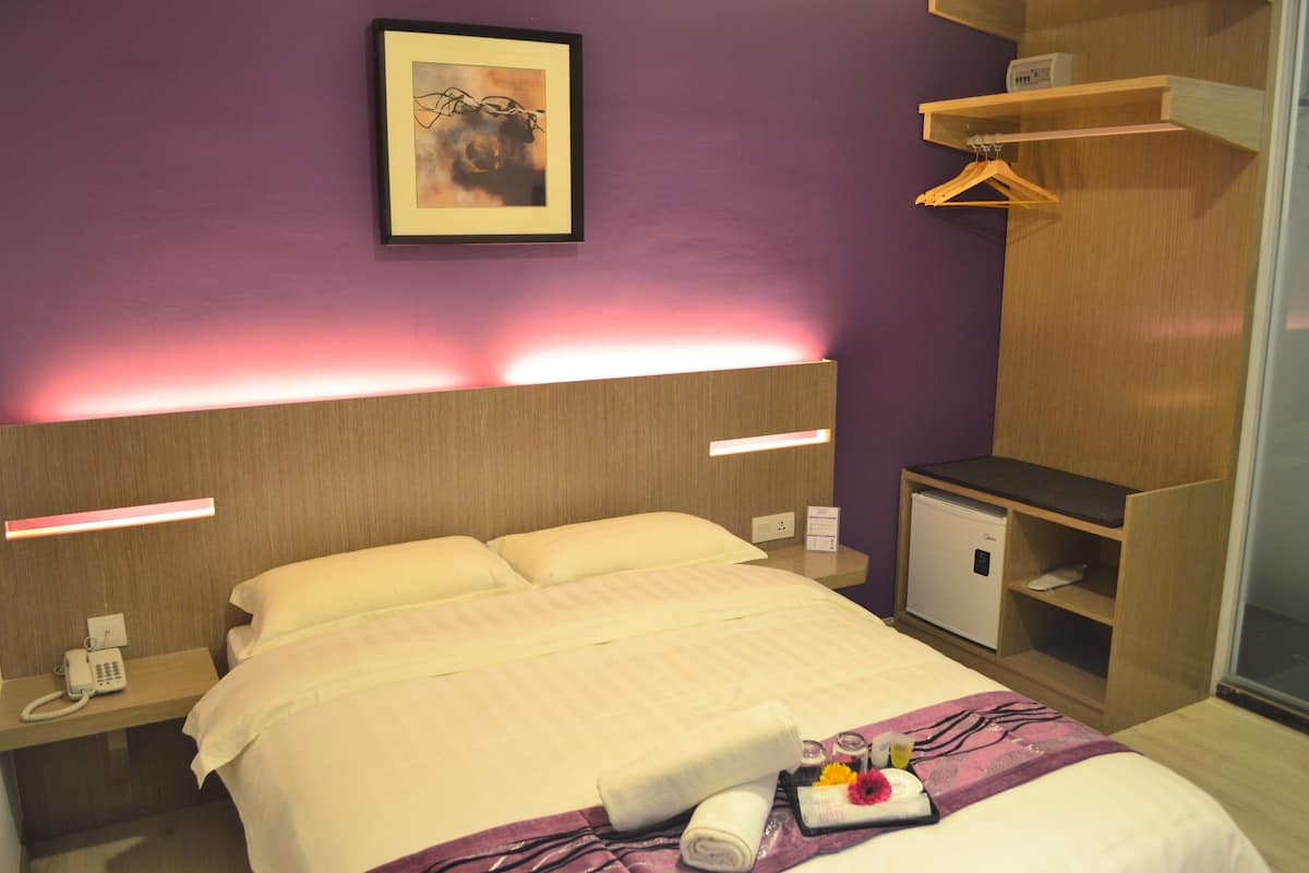 Quarto de hotel com cama, mesas de cabeceira, mini-frigorífico, prateleira de madeira e quadro na parede.