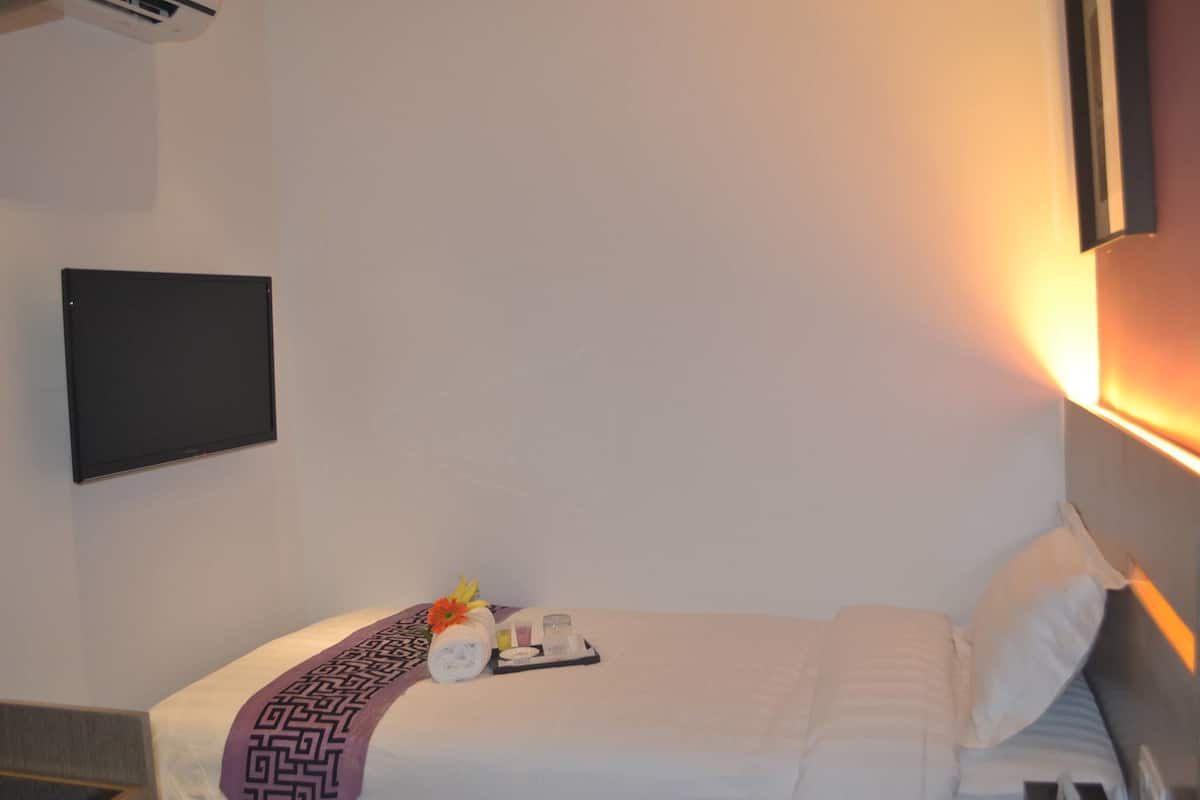 Quarto de hotel com uma cama, televisão de tela plana na parede e mesa de cabeceira com um kit de higiene pessoal.