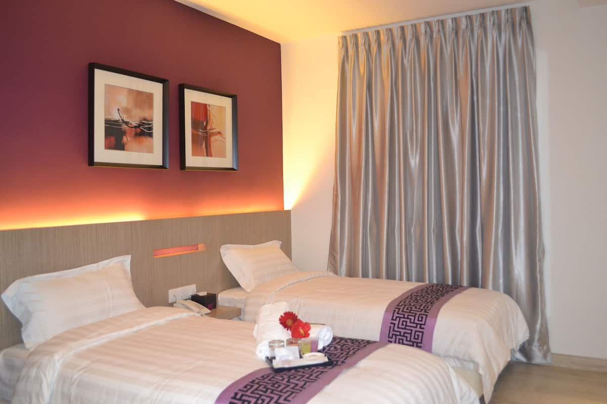 Quarto de hotel com duas camas, uma mesinha de cabeceira com telefone e um porta-bandeja com artigos de higiene pessoal.