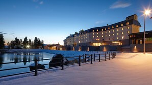 Um hotel com um prédio grande, terreno coberto de neve e um corpo d'água.