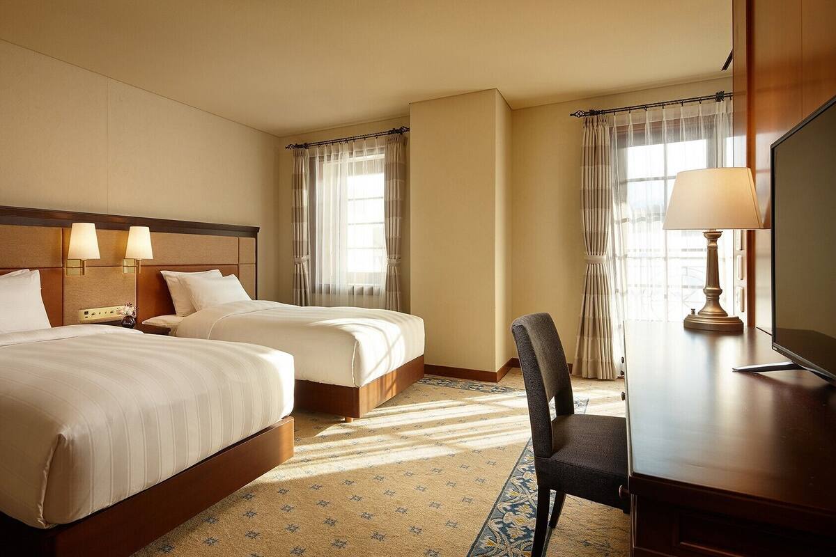 Quarto de hotel com duas camas, uma escrivaninha, uma cadeira e uma televisão.