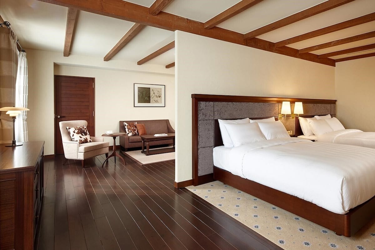 Quarto de hotel com duas camas, um sofá, uma poltrona e uma escrivaninha.