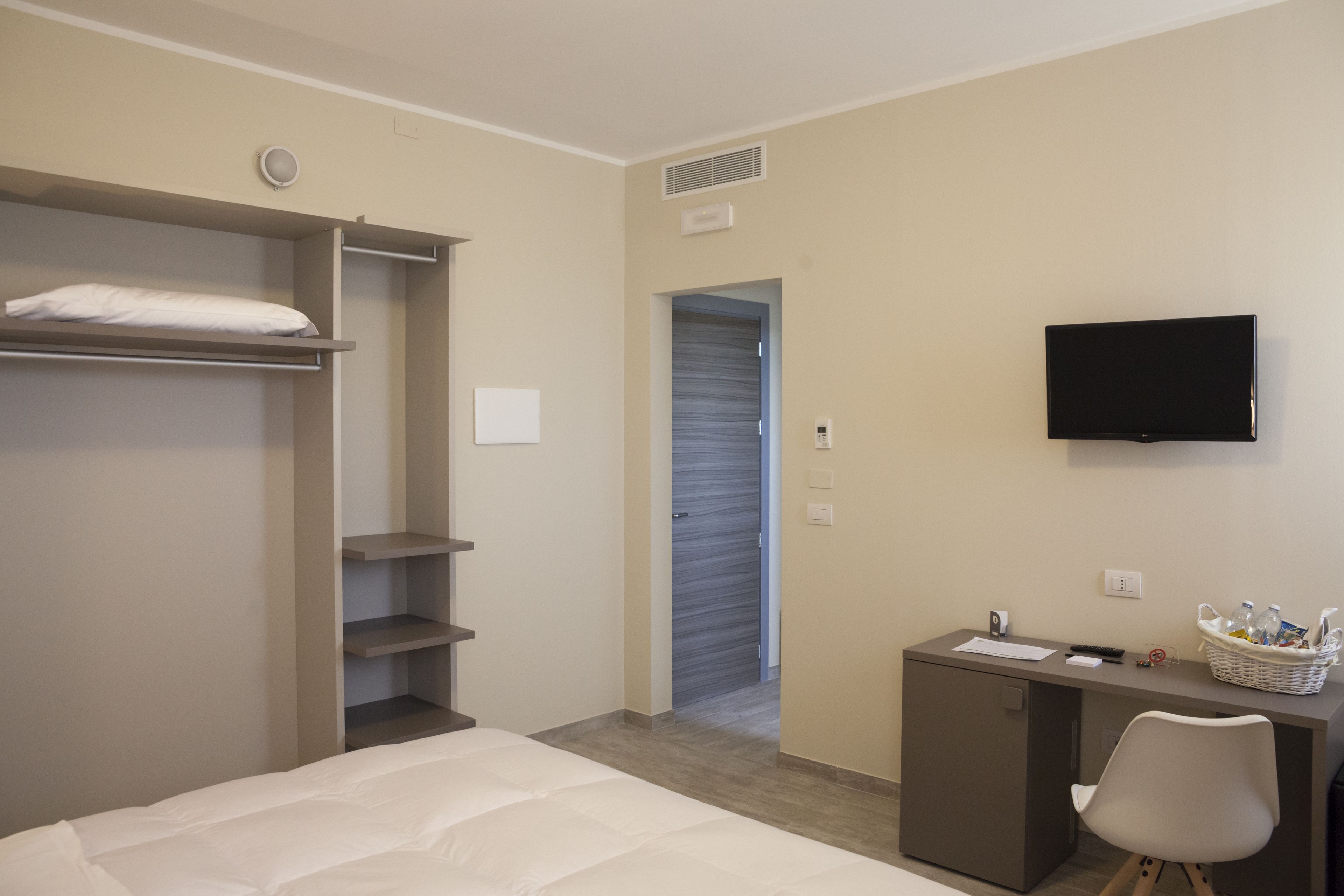 Quarto de hotel com cama, escrivaninha, televisão e armário.