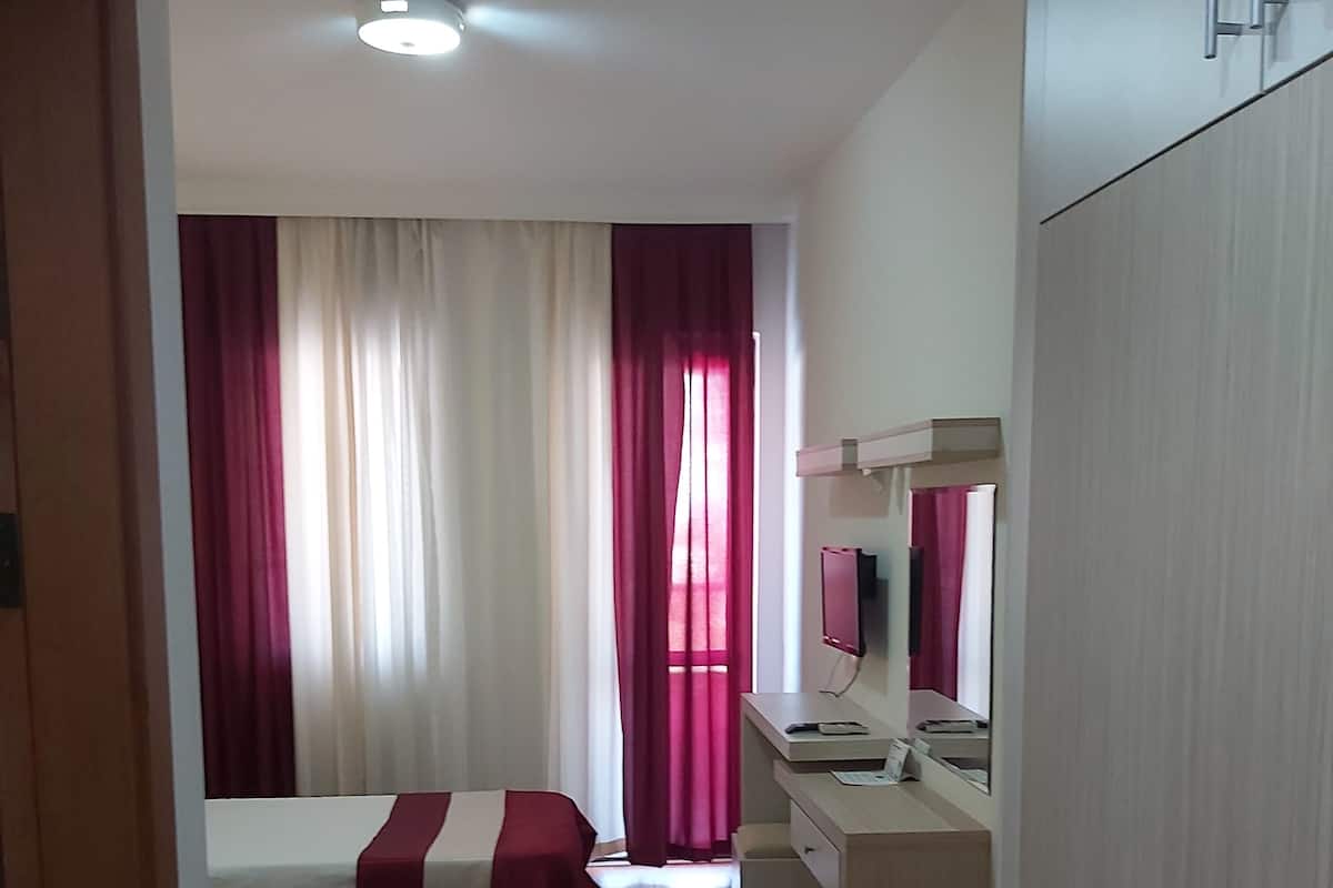 Quarto com duas camas, uma escrivaninha, um espelho e um guarda-roupa.