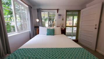 Quarto de hotel com uma cama, janela com cortinas, uma porta e um painel de avisos na parede.