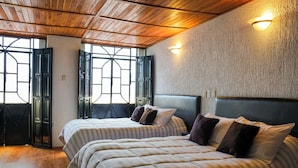 Quarto de hotel com duas camas, teto de madeira, janelas amplas e parede com textura.