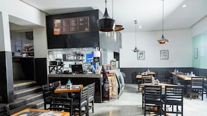 Interior moderno de restaurante com várias mesas e cadeiras, um balcão com menu exposto e luminárias pendentes.
