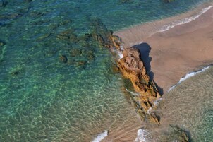Paisagem costeira com águas cristalinas, uma praia de areia e afloramentos rochosos.