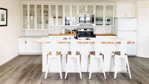Uma cozinha moderna com armários brancos, uma ilha central com banquetas e um claraboia.