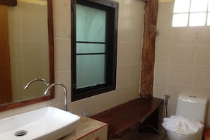 Uma casa de banho com lavatório branco, espelho, janela, toucador de madeira e sanita.