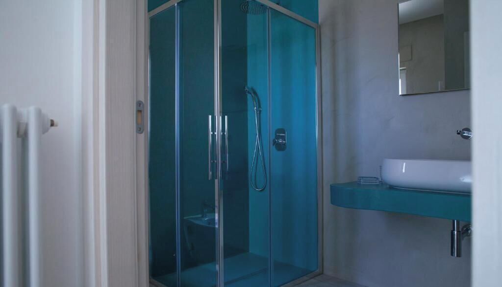 Casa de banho com chuveiro em cabine de vidro, lavatório branco e espelho sobre o lavatório.