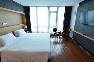 Quarto de hotel com uma cama grande, televisão, escrivaninha e uma cadeira.