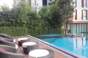 Piscina com deck ladrilhado, cercada por vegetação e edifícios modernos.