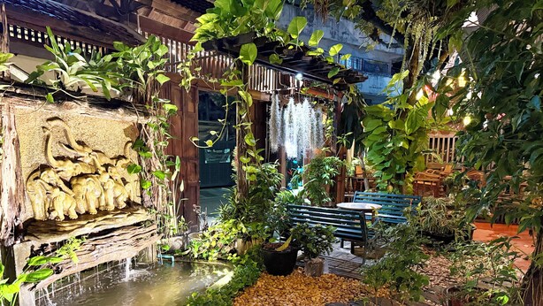 Um jardim interno tranquilo com fonte de água, bancos de madeira e vegetação exuberante.