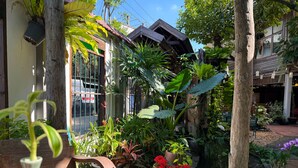 Uma área de jardim com diversas plantas, um pequeno lago com peixes e uma mesa de madeira com um vaso.