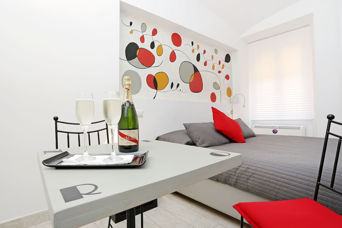 Quarto moderno com uma cama, uma mesa com uma garrafa de champanhe e uma parede decorada com arte abstrata.