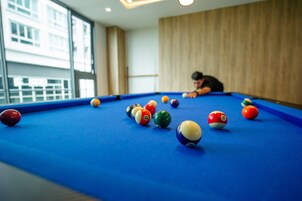Uma mesa de bilhar com bolas em um espaço com grandes janelas e painéis de madeira.