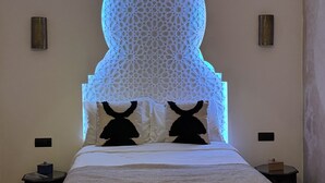 Uma cama com cabeceira estampada em branco e preto, duas mesas de cabeceira e uma luminária decorativa no teto.