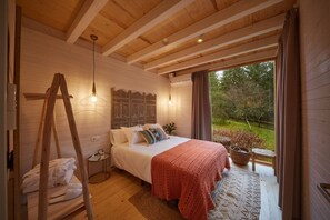 Um quarto aconchegante com teto de madeira, uma cama com cobertor vermelho, uma escada de madeira e vista para um jardim através de uma janela grande.