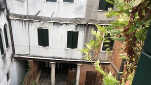 Um pátio com área de estar, um edifício com várias janelas e alguma vegetação.