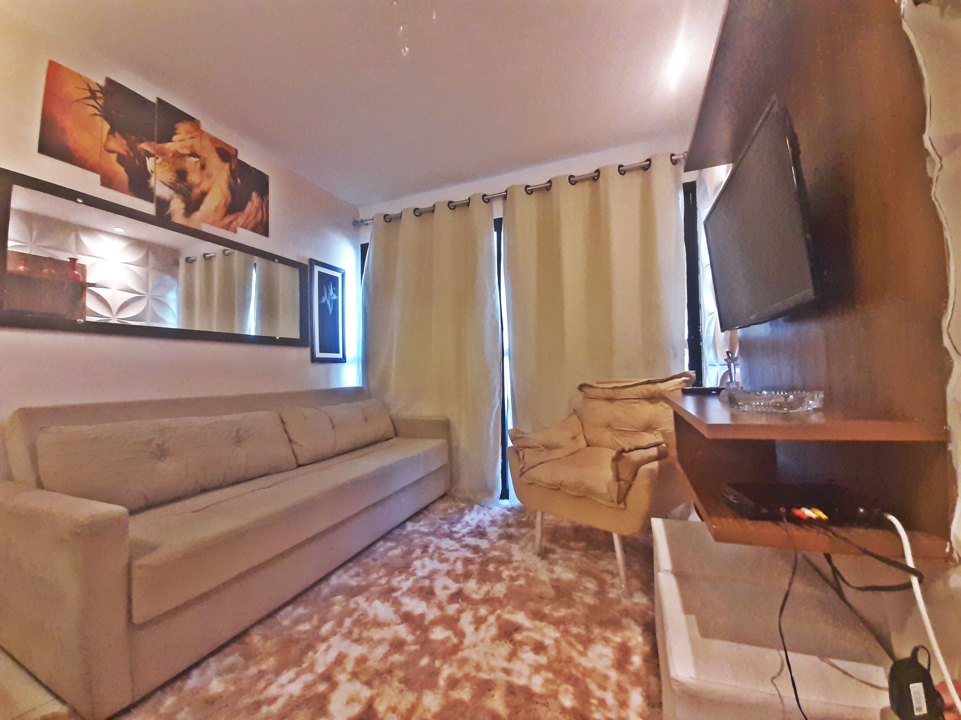 Uma sala de estar com um sofá, uma televisão sobre um móvel, um espelho e uma parede decorada com obras de arte.