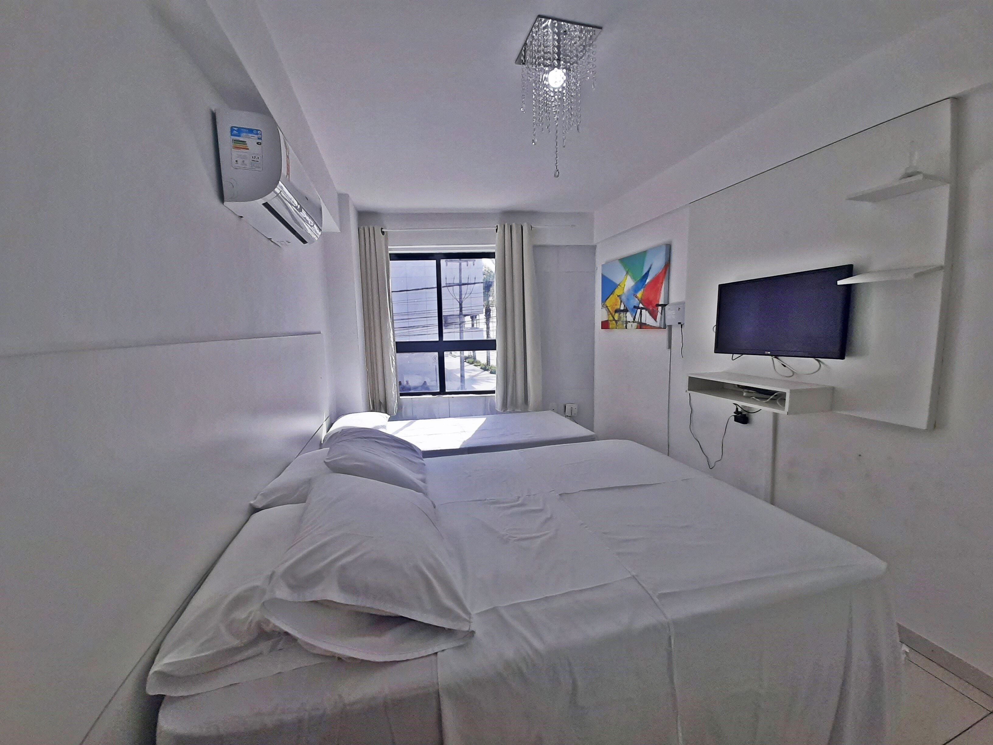 Quarto de hotel com uma cama, uma televisão presa à parede e uma janela com cortinas.