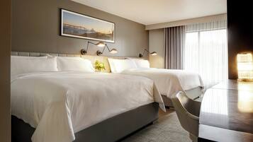 Quarto de hotel com duas camas, uma escrivaninha e uma janela grande com cortinas.