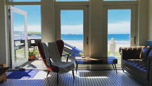 Quarto com vista para a praia, uma cadeira vermelha, um sofá castanho e uma pequena mesa.