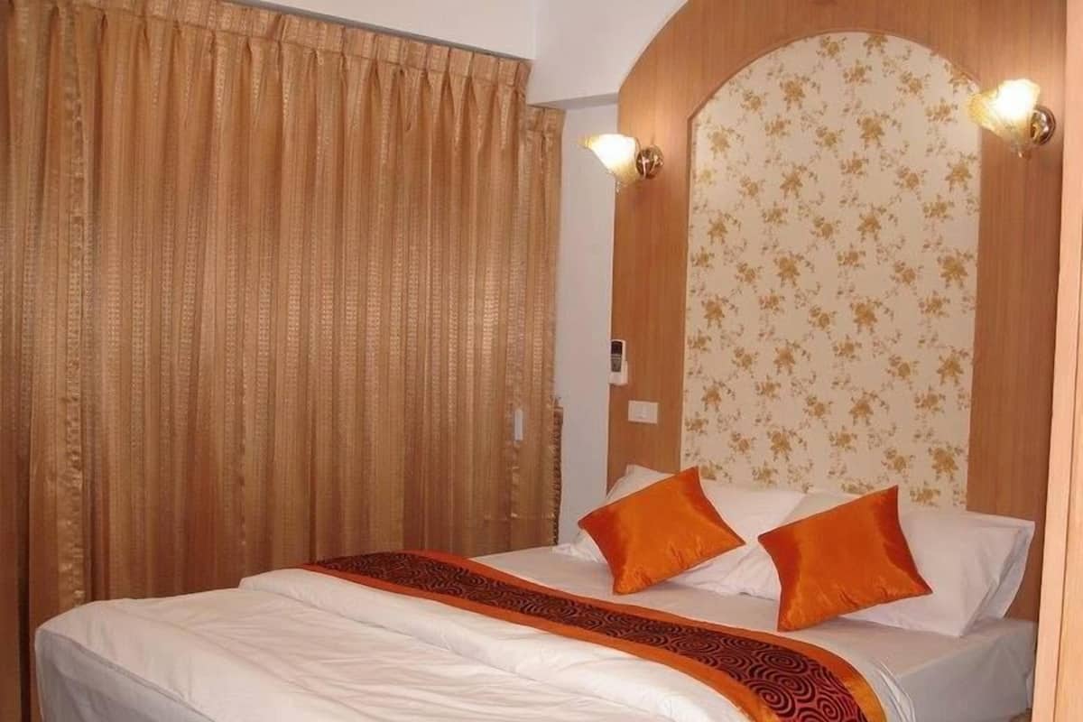 Quarto de hotel com cama, cortinas, luminária na parede e papel de parede estampado.