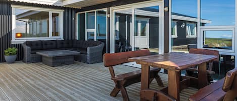 Um deck externo com mesa e bancos de madeira, um sofá e um vaso de planta.