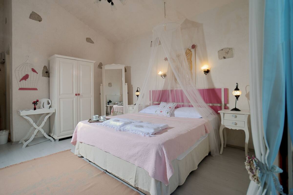 Quarto com cama de dossel, guarda-roupa, penteadeira e pequena mesa com abajur.