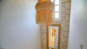 Uma escadaria com corrimão branco, luminária de palha trançada e espelho com moldura decorativa.