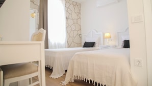 Quarto de hotel com duas camas, uma cadeira, um abajur e parede com padrão de pedra.