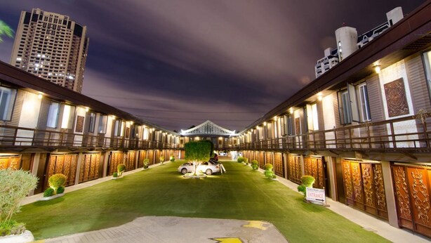 Um hotel com fachada simétrica, entrada central e gramado bem cuidado.