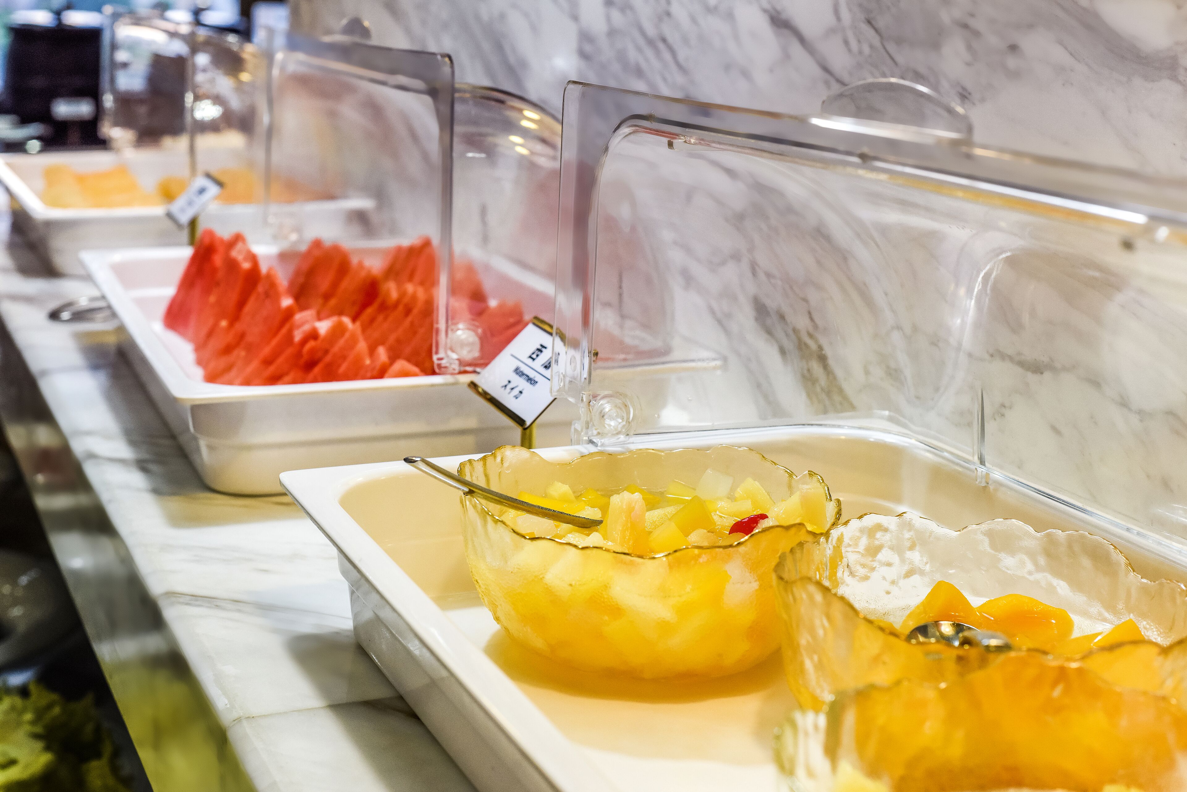 Buffet com diversos alimentos em recipientes transparentes.