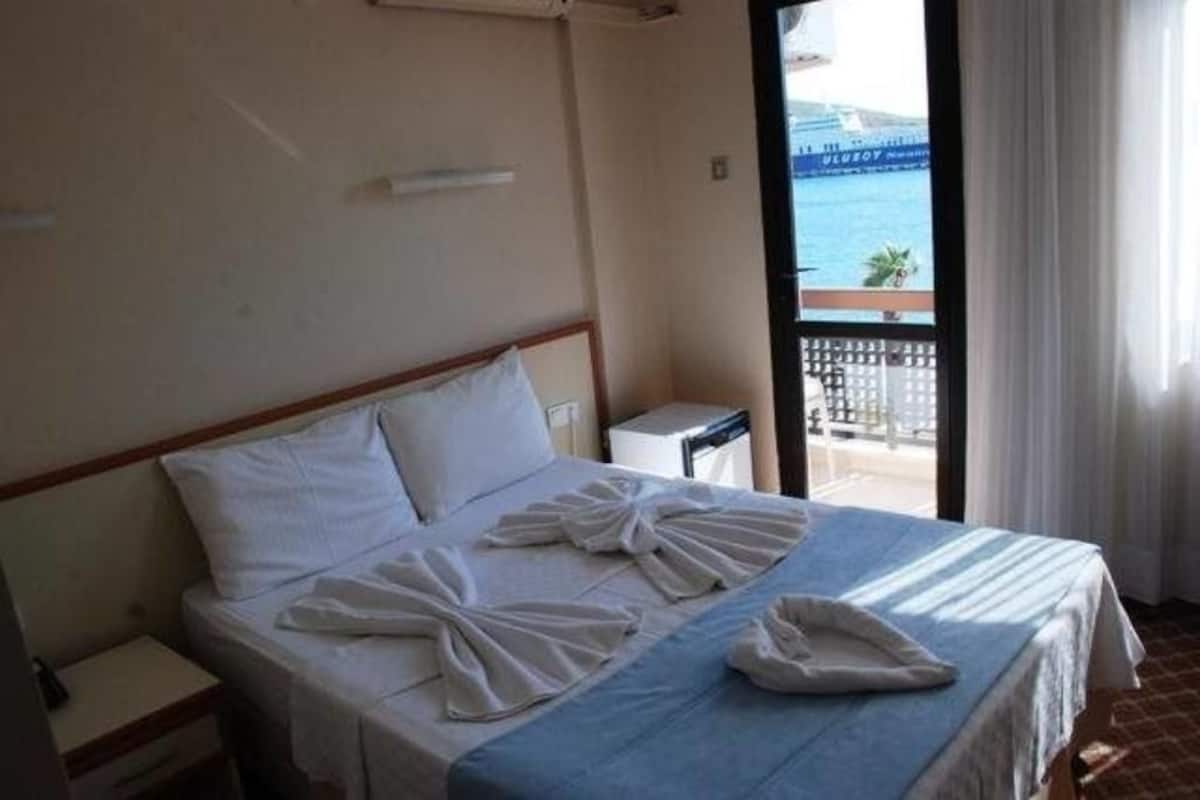 Quarto de hotel com uma cama, uma mesa de cabeceira, uma pequena mesa e vista para o mar através de uma porta varanda.