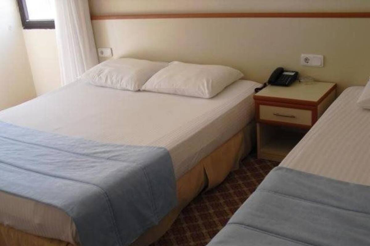 Quarto de hotel com uma cama de solteiro, mesa de cabeceira com telefone e janela com cortinas.