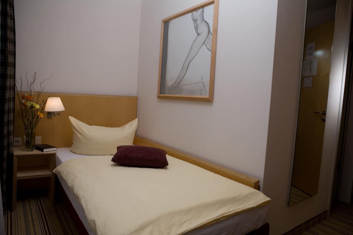 Quarto de hotel com uma cama, mesa de cabeceira, luminária, obra de arte emoldurada e um espelho.