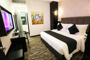 Quarto de hotel com uma cama grande, uma mesa com computador, uma TV e um quadro na parede.