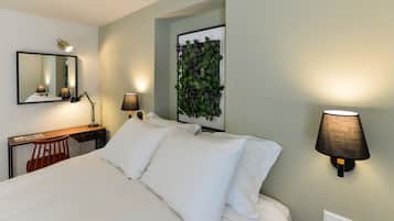 Quarto de hotel com cama, escrivaninha, cadeira, abajur e planta fixada na parede.