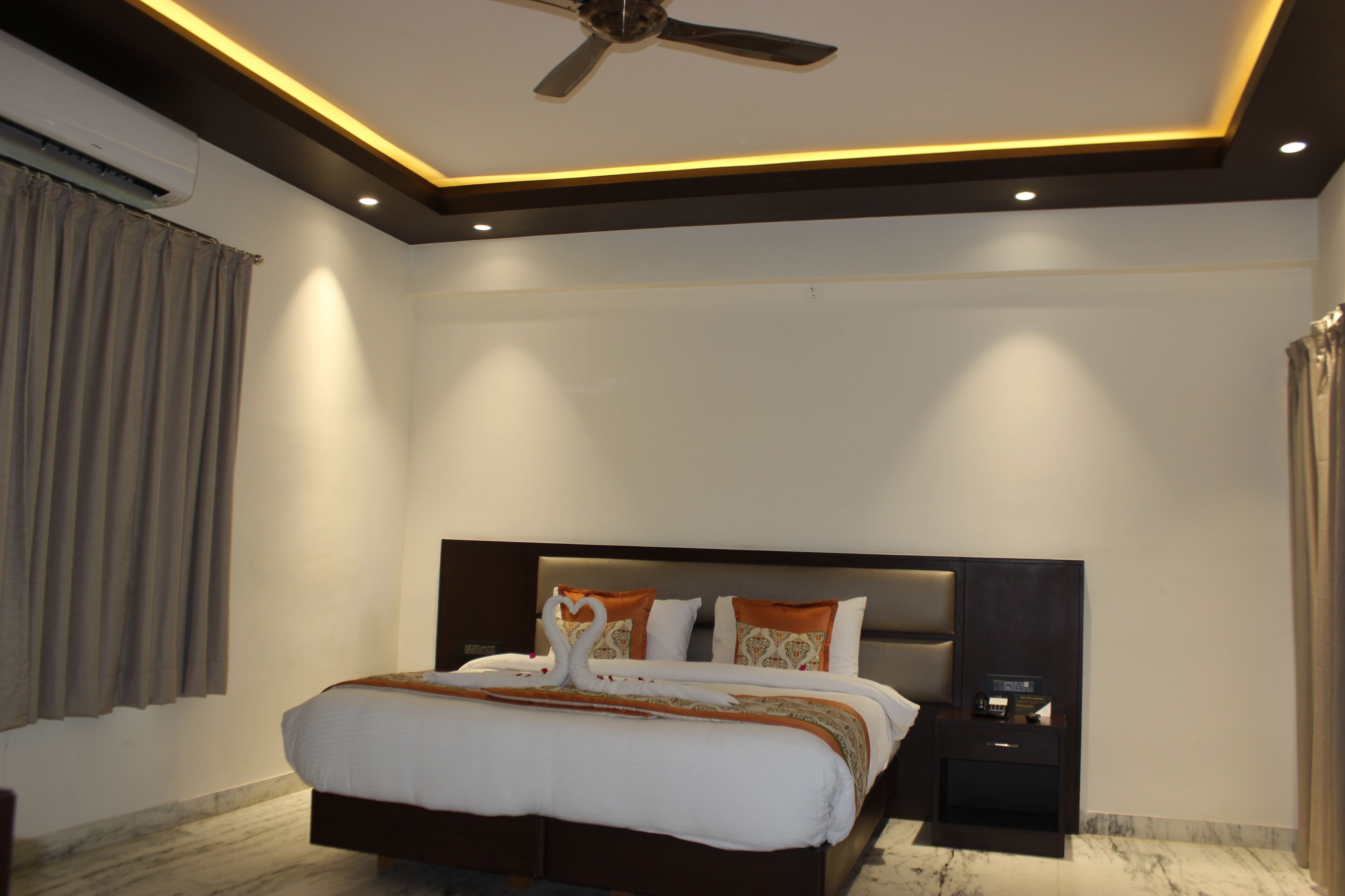 Quarto de hotel moderno com uma cama grande, uma mesinha de cabeceira e um ventilador de teto.