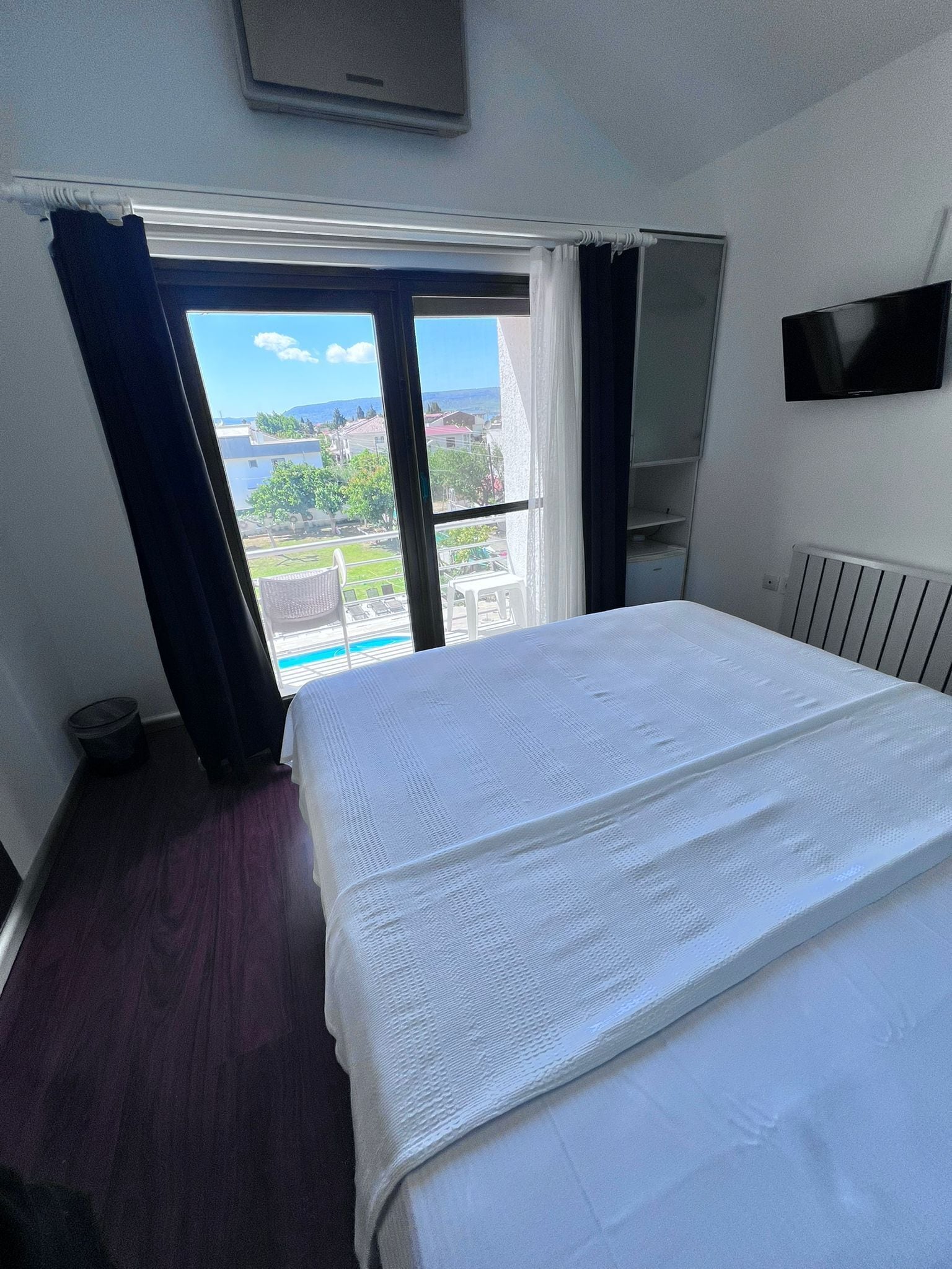 Quarto de hotel com cama, televisão, janela com cortinas e vista para o exterior.