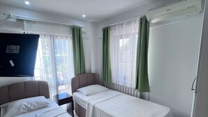 Quarto de hotel com duas camas, televisão de tela plana, ar-condicionado no teto e uma janela com cortinas translúcidas.