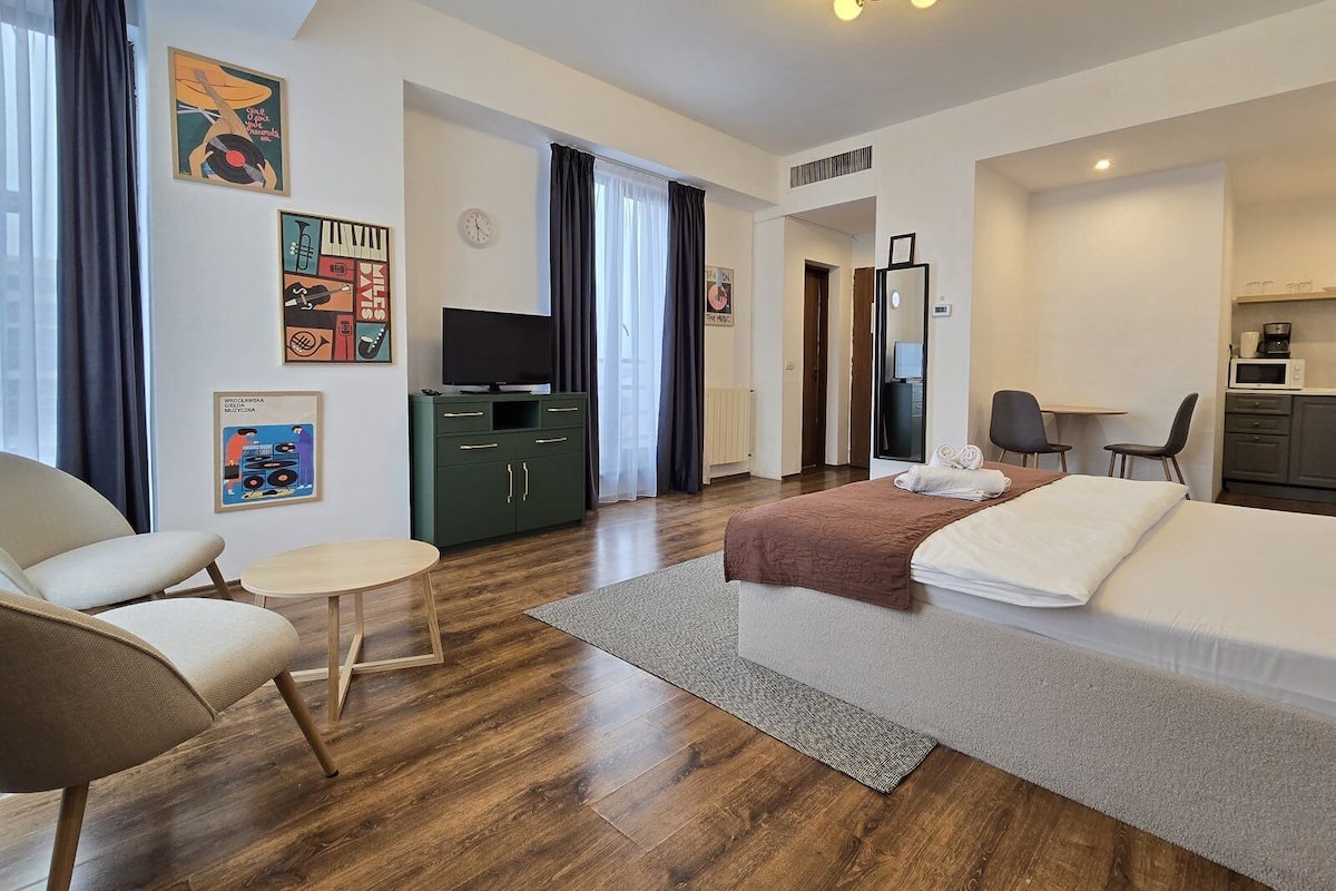 Quarto de hotel moderno com cama, escrivaninha, cadeira, televisão e obras de arte nas paredes.