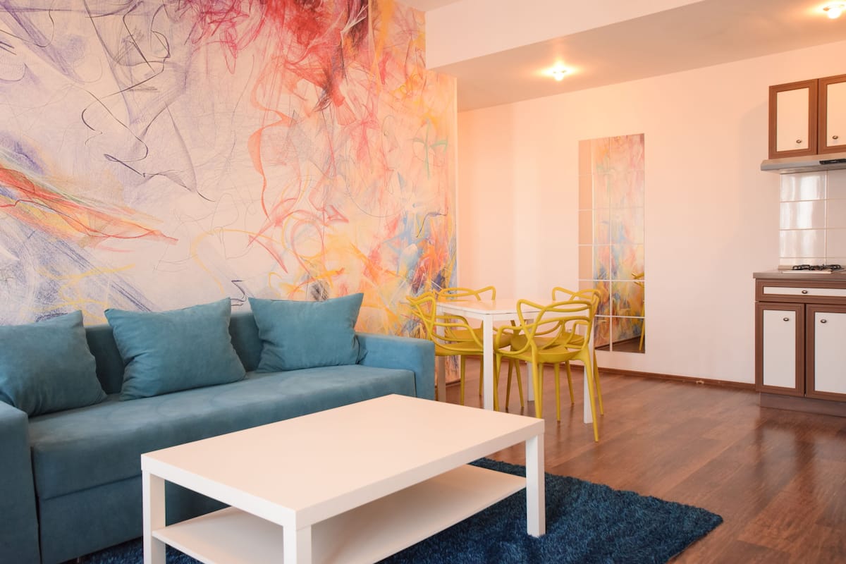 Uma sala de estar moderna com sofá, mesa de centro e área de jantar com cadeiras amarelas.