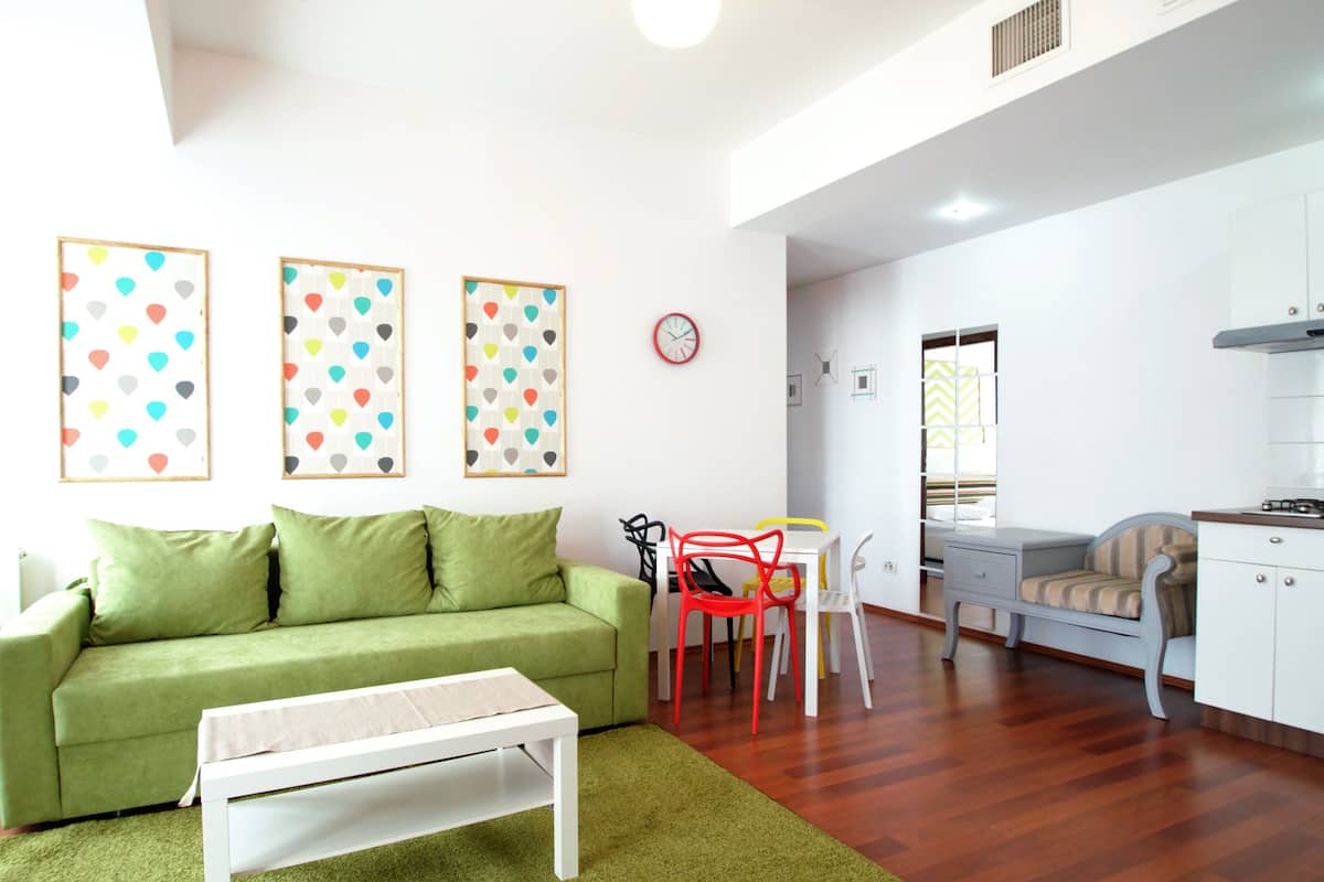 Uma sala de estar moderna com um sofá verde, uma mesa de centro branca e arte de parede com padrão de corações.