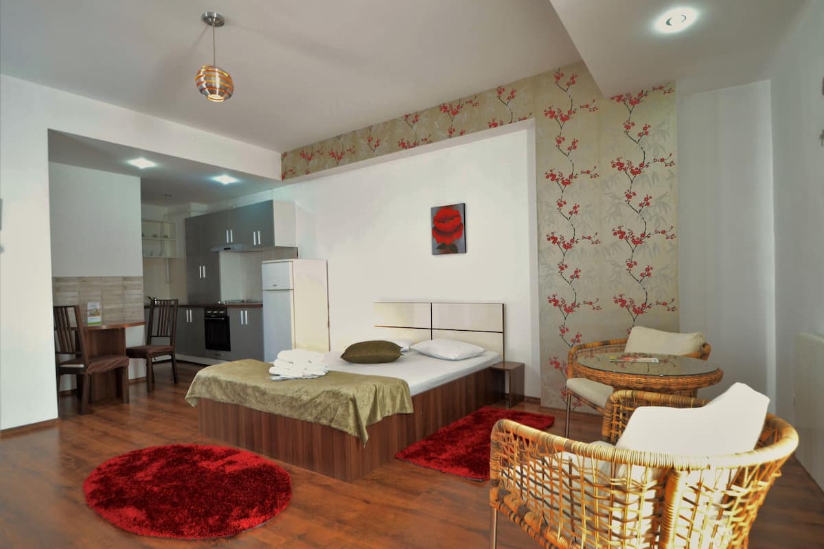 Um quarto moderno com cama, uma mesinha redonda, cadeiras de vime e um tapete vermelho.