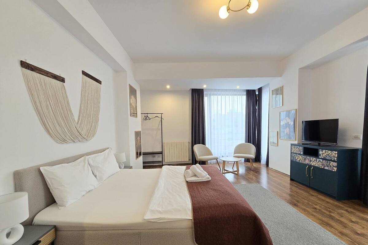 Quarto de hotel moderno com uma cama grande, uma escrivaninha, uma cadeira, uma televisão e um guarda-roupa.