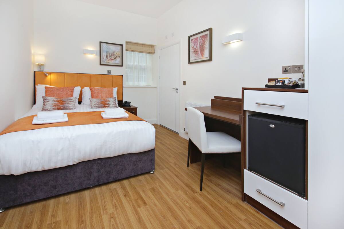 Quarto de hotel com cama, escrivaninha, cadeira e forno embutido.