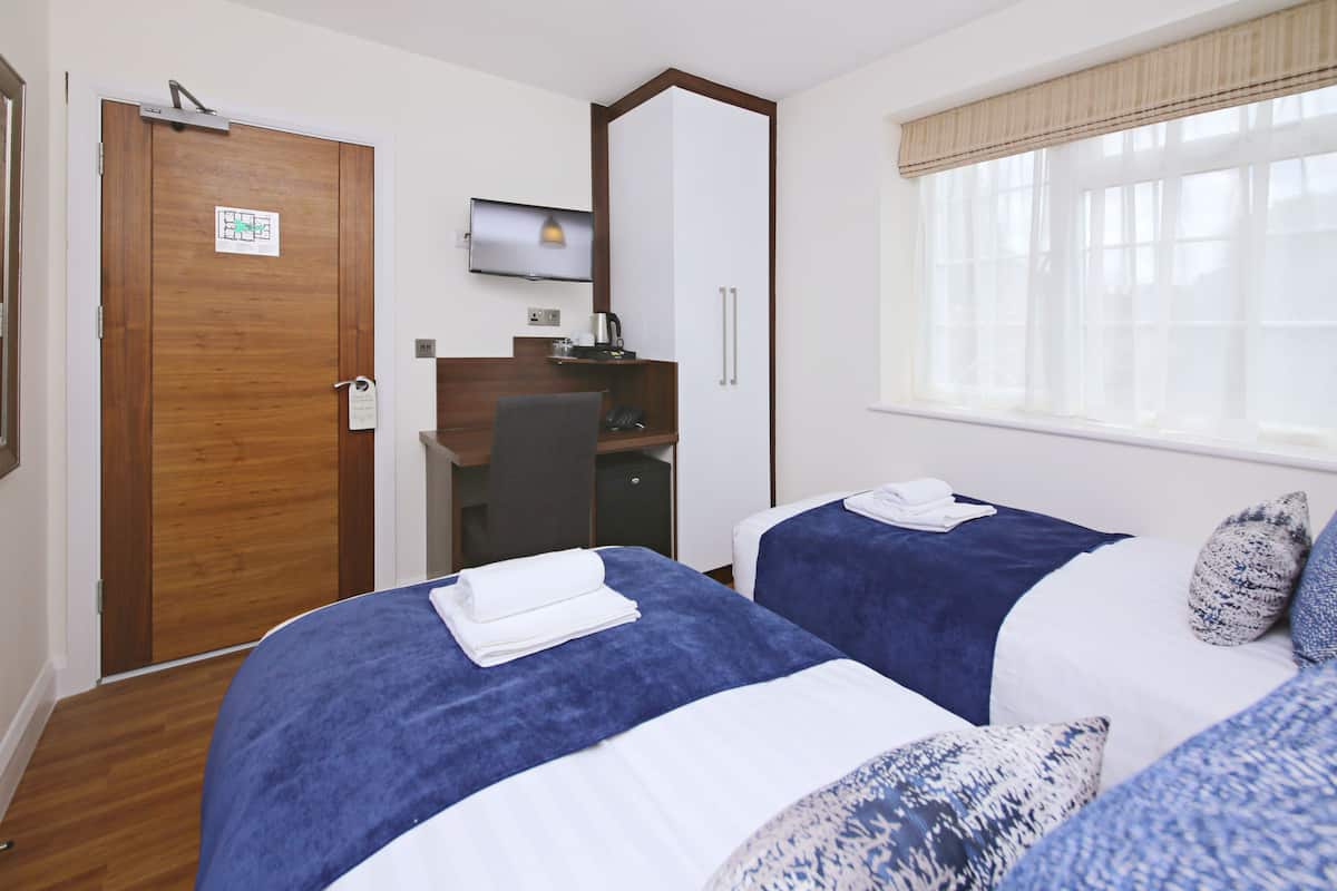Quarto de hotel com duas camas, uma escrivaninha, uma televisão e uma janela com persianas.